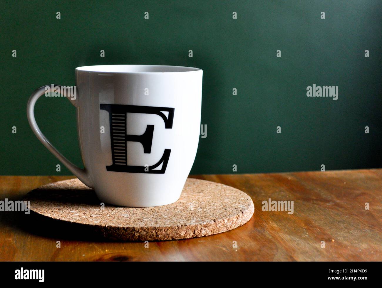 Large white mug with the letter 'E' on a cork mat on a wooden table set ...