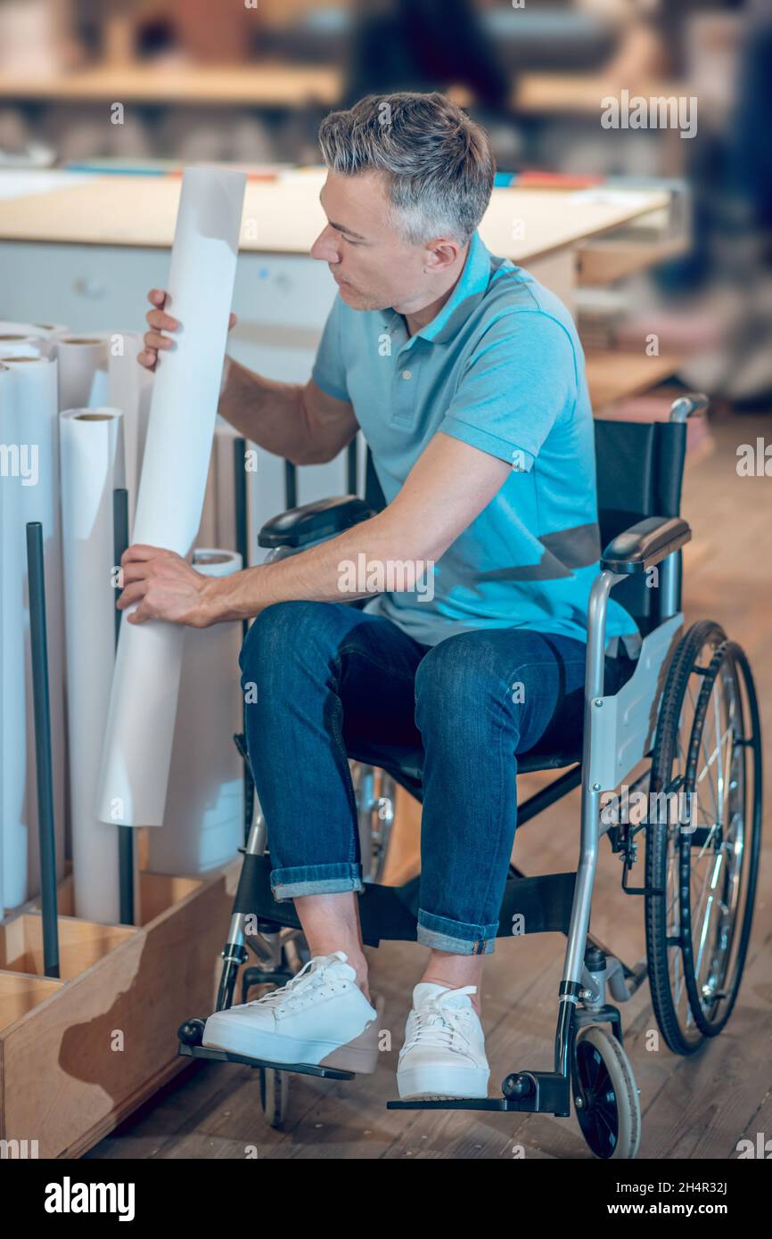 Man in wheelchair taking roll of paper Stock Photo - Alamy