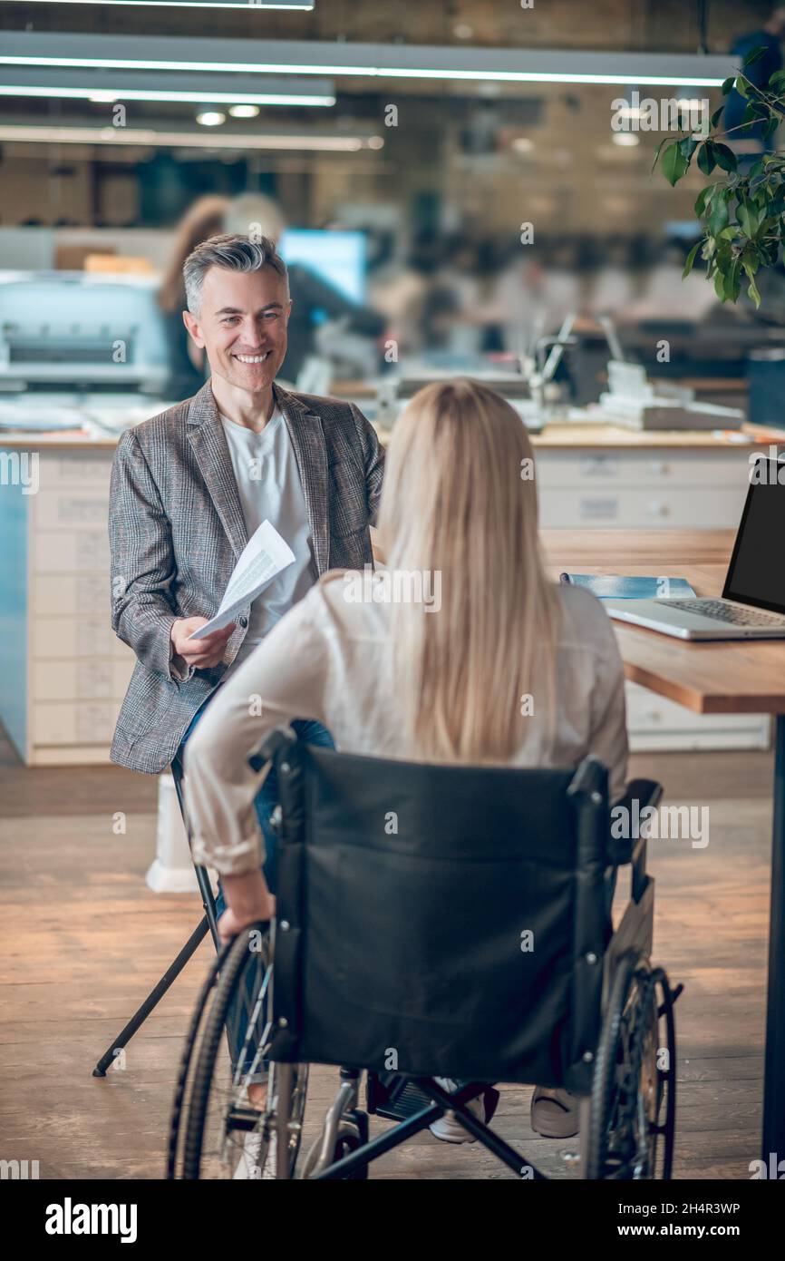 Man stretching papers to woman in wheelchair Stock Photo - Alamy