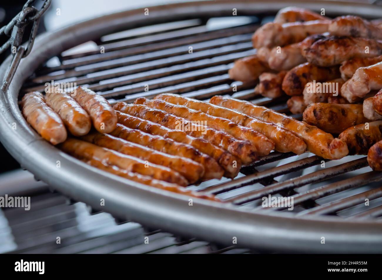 Process of grilling fresh meat sausages on big round hanging grill ...