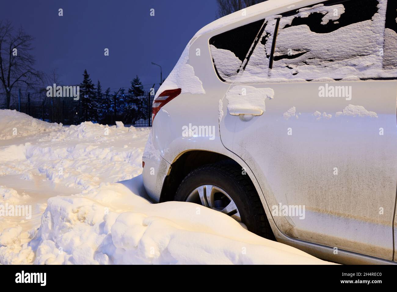 White car covered with snow at night. Parked SUV in the yard. City ...