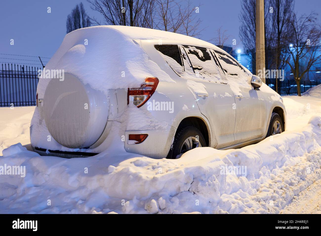 White car covered with snow at night. Parked SUV in the yard. City ...