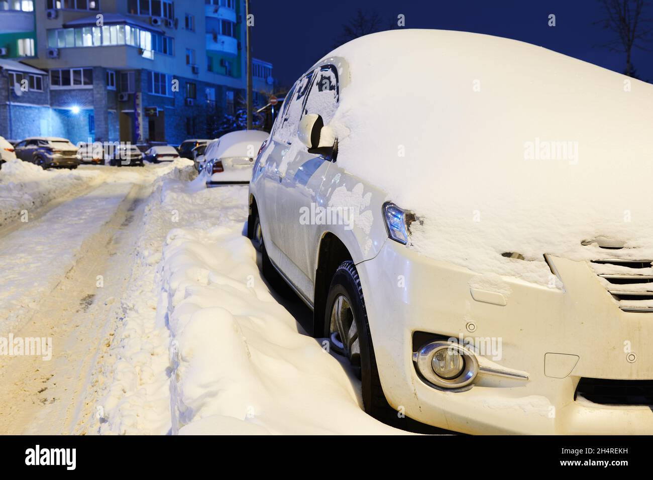 White car covered with snow at night. Parked car in the yard. City ...
