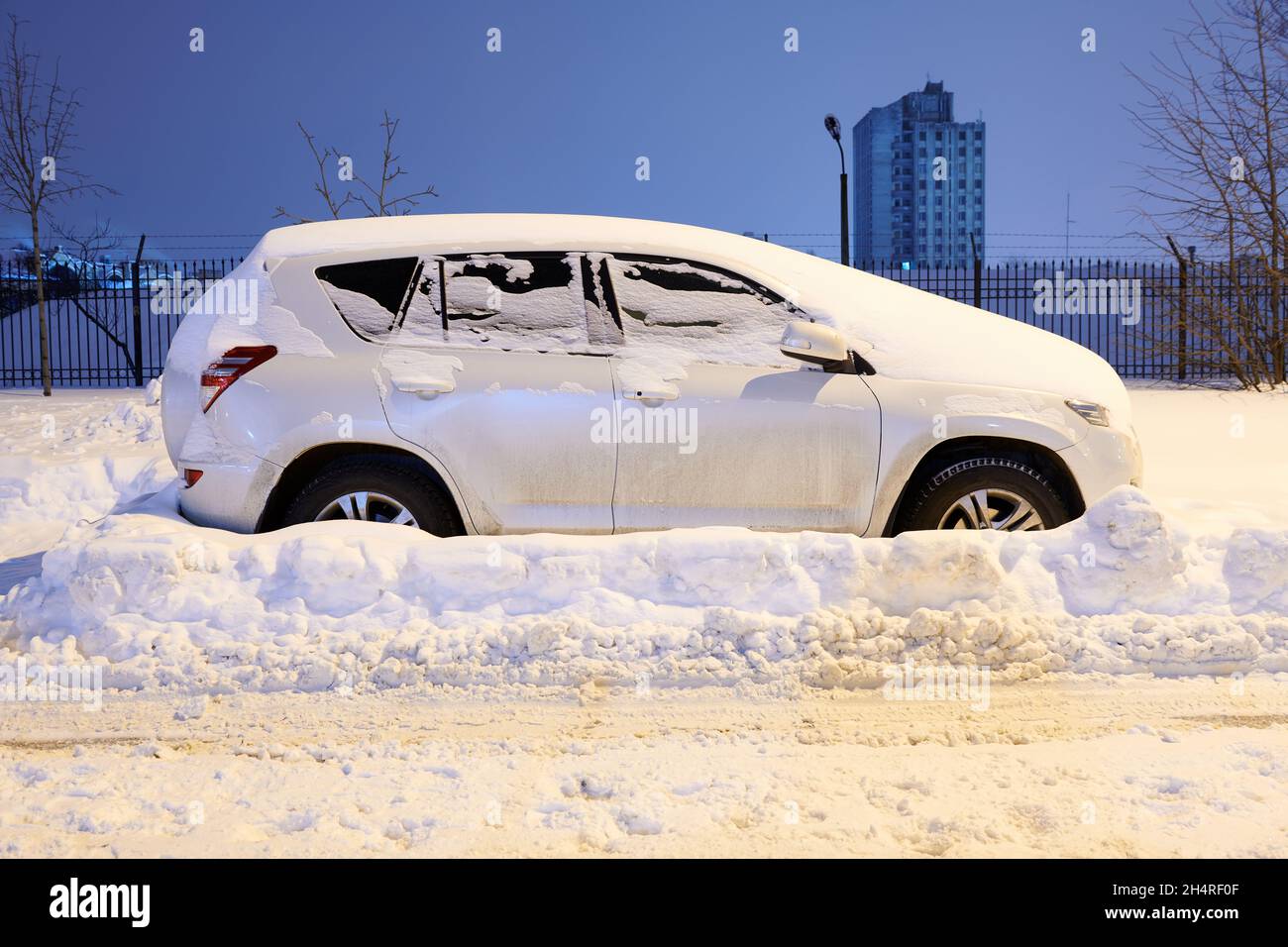 White car covered with snow at night. Parked car in the yard. City ...