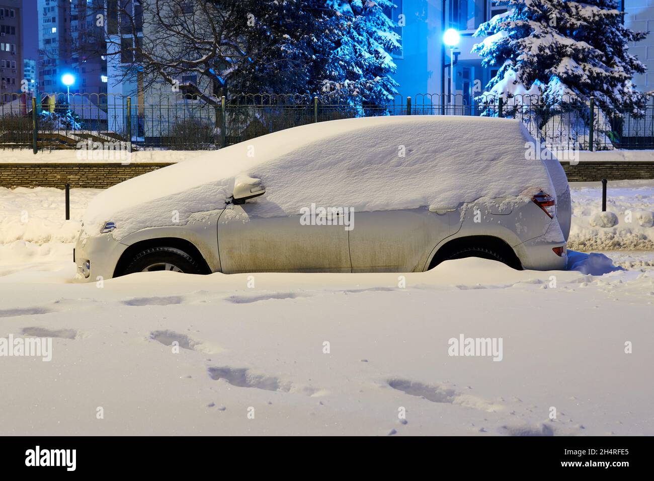White car covered with snow at night. Parked car in the yard. City ...