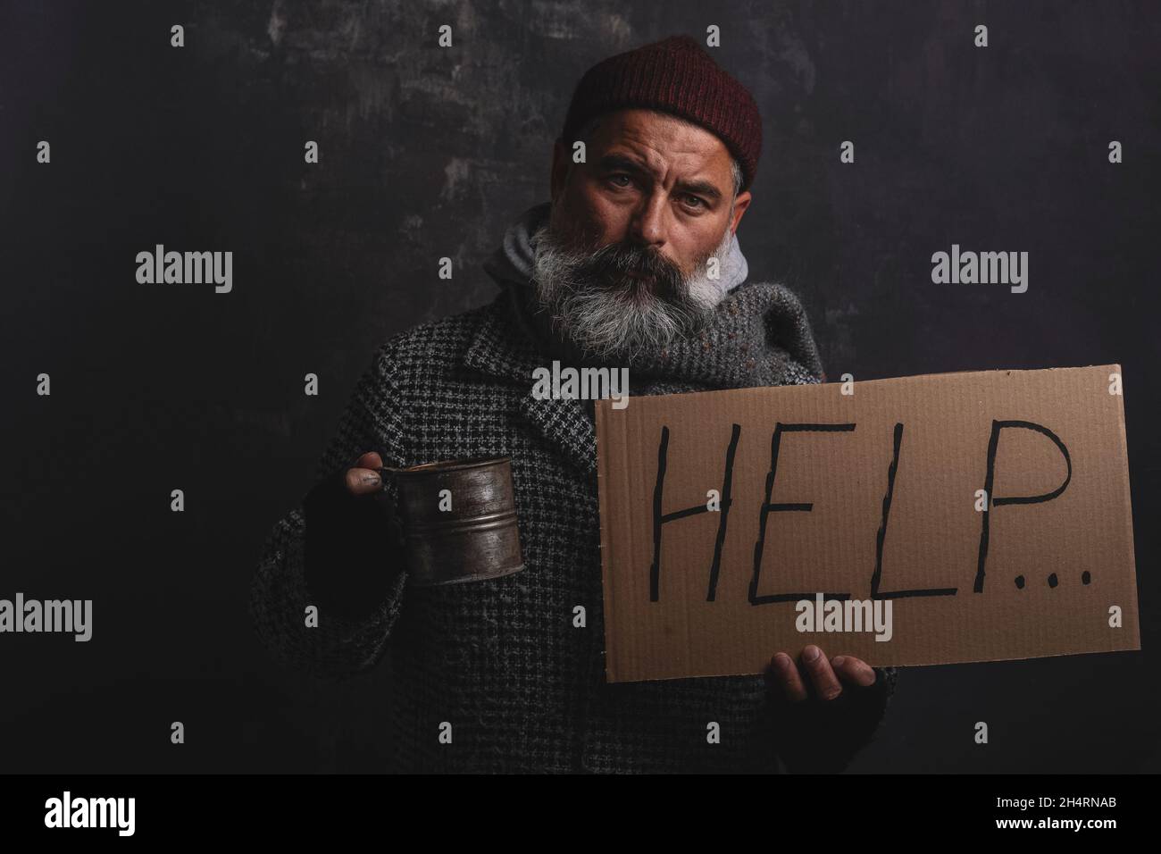 Portrait of poor homeless man with poster and a pot for alms on a dark ...