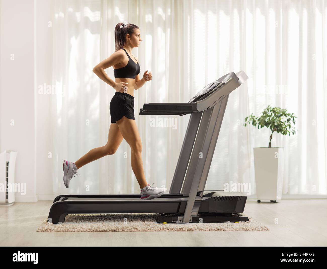 Full length profile shot of a fit young woman running on a treadmill at ...