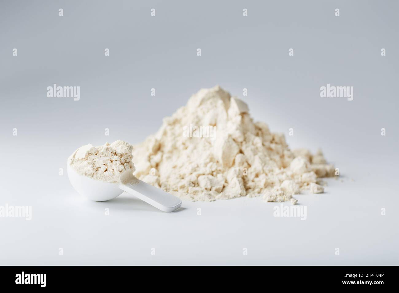 A pile of protein powder with a measuring spoon on a white background ...