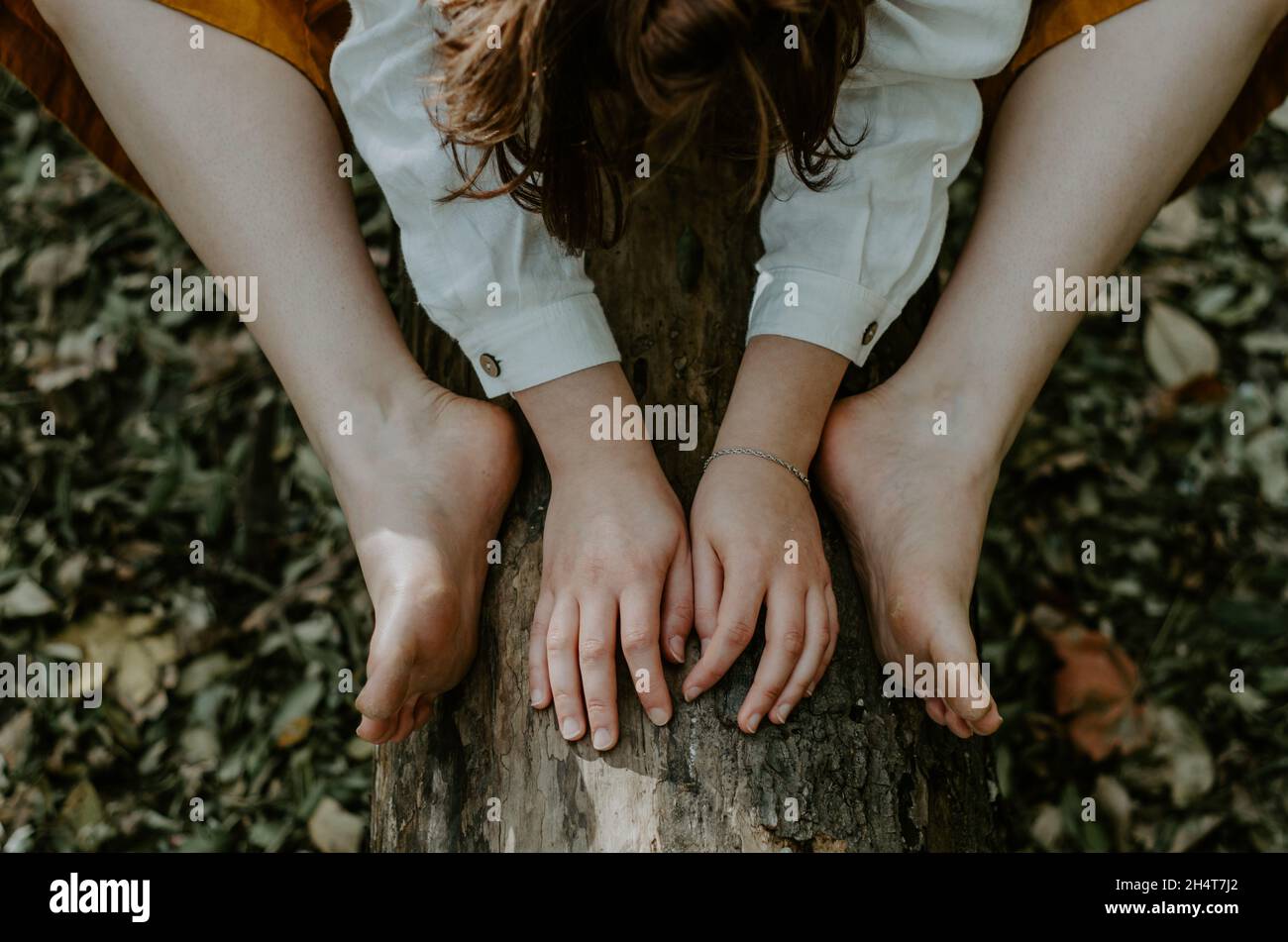 Details of woman seated on fallen tree with bare feet and hands on tree ...