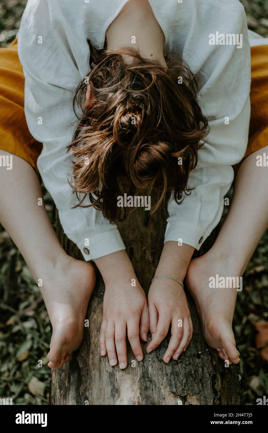 Vertical photo, details of woman seated on fallen tree with bare feet ...