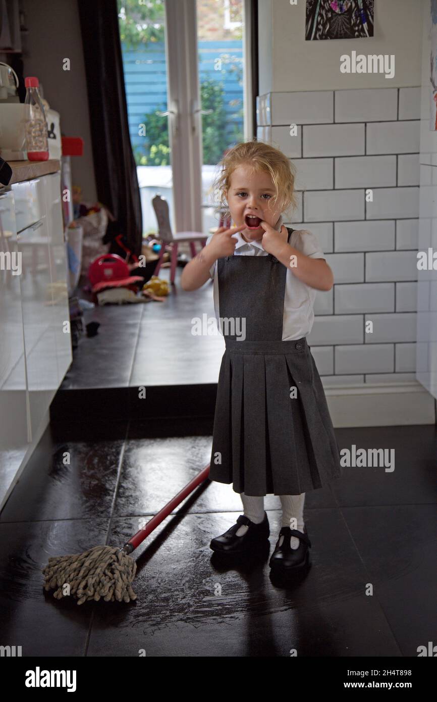 A 3 year old girl in school uniform mopping the kitchen floor, UK Stock ...
