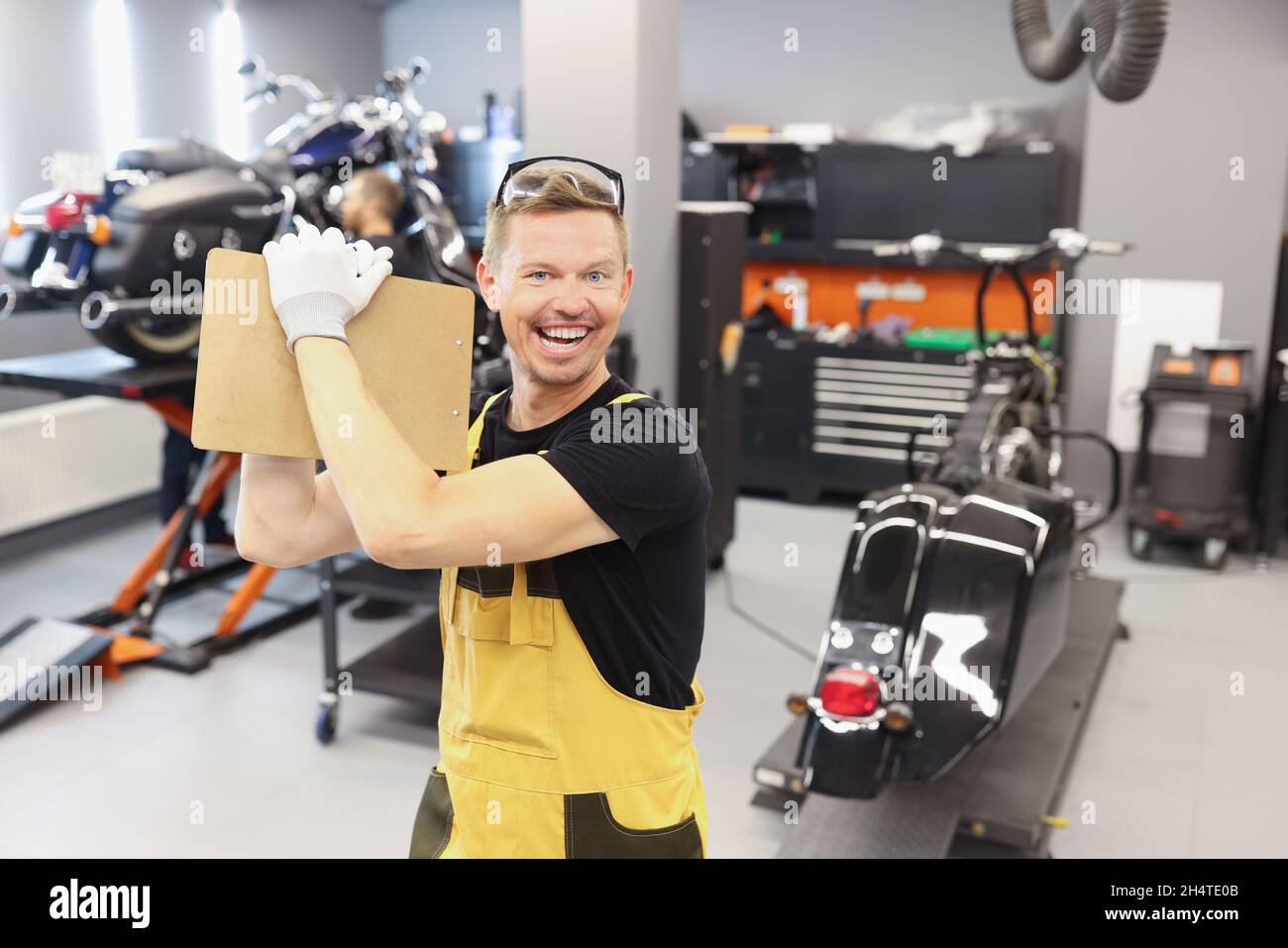 Happy male repairman holding clipboard with documents near motorcycle ...