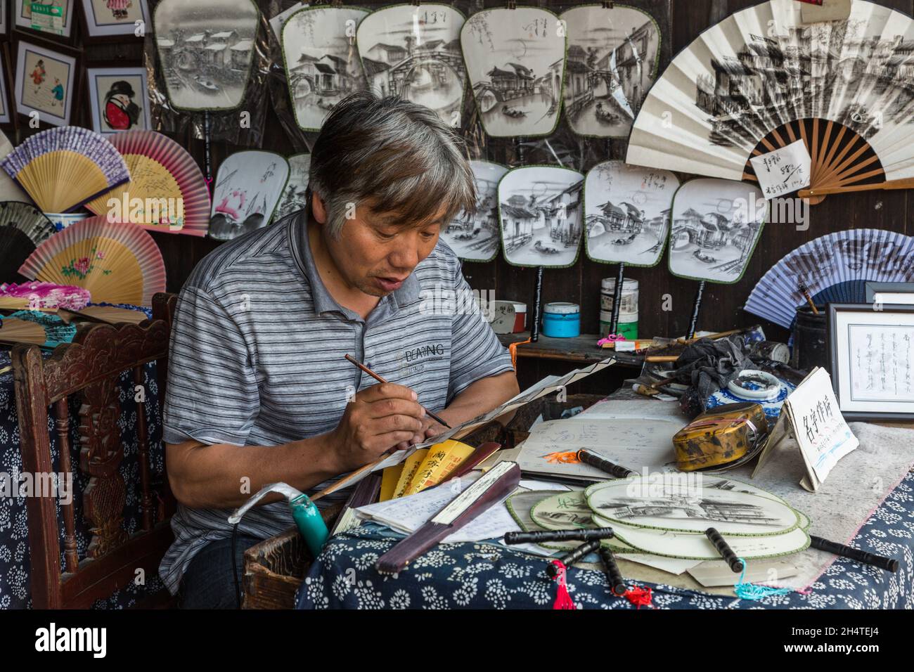 A Chinese man paints traditional scenes on fans in his shop in Wuzhen ...