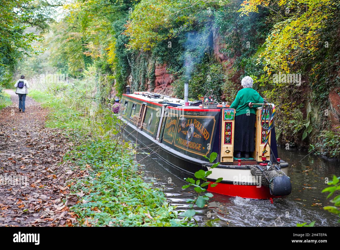 Rear view of a narrowboat travelling along a UK canal with senior lady ...