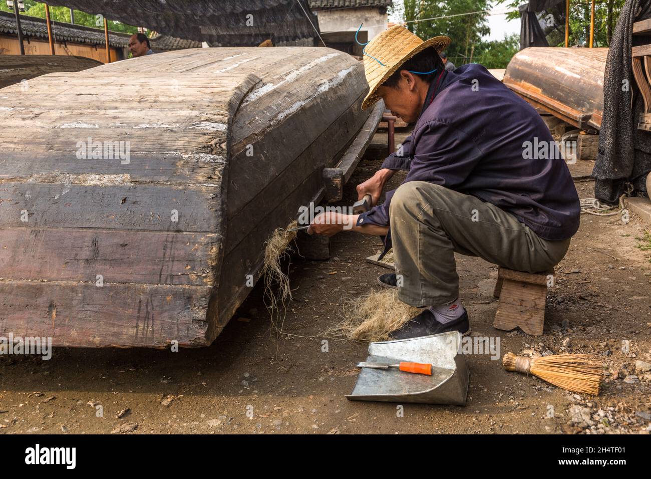 A Chinese craftsman repairs a traditional wooden boat in a boatyard in ...