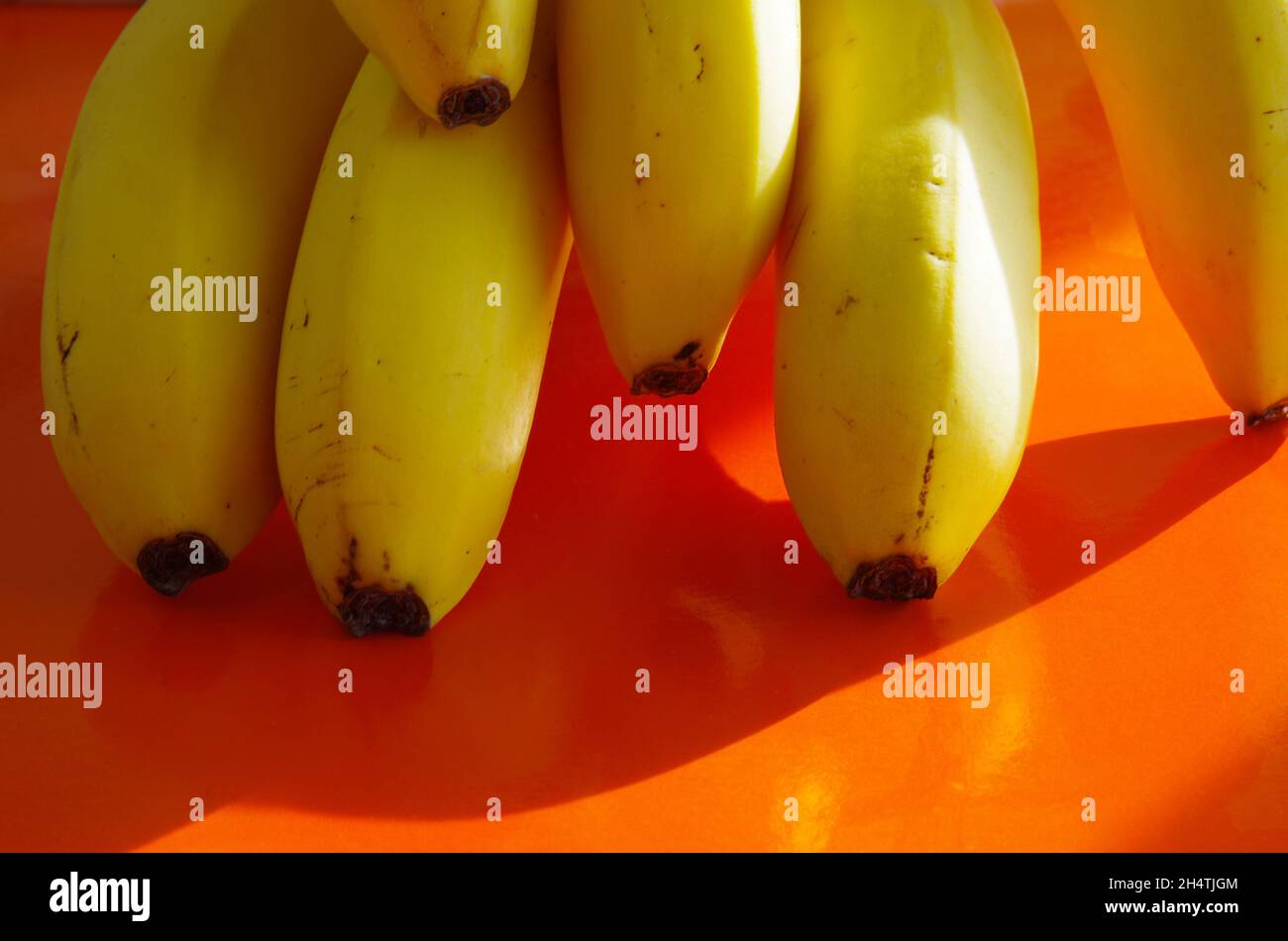 Ripe bananas lit by the sun on an orange background Stock Photo - Alamy