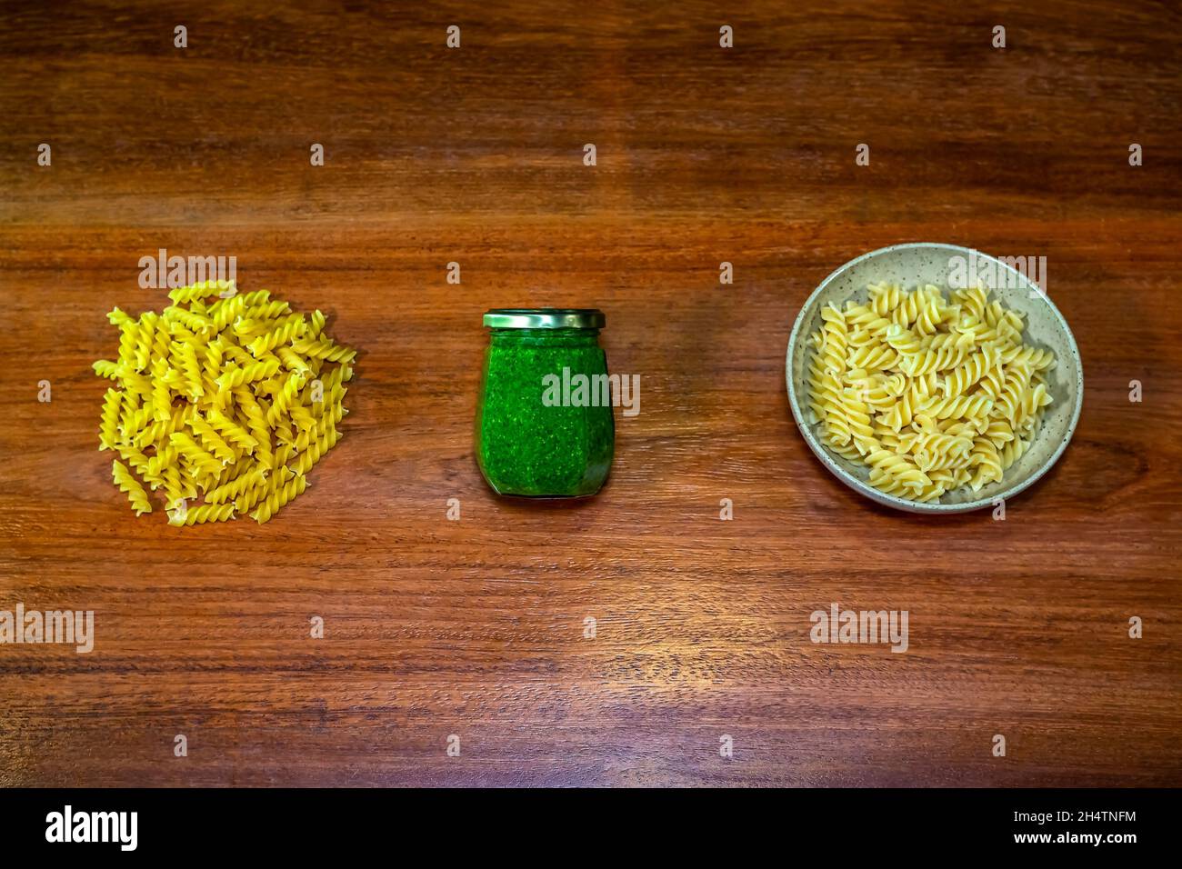 Stack of uncooked fusilli pasta, pesto, and cooked fusilli pasta dish ...