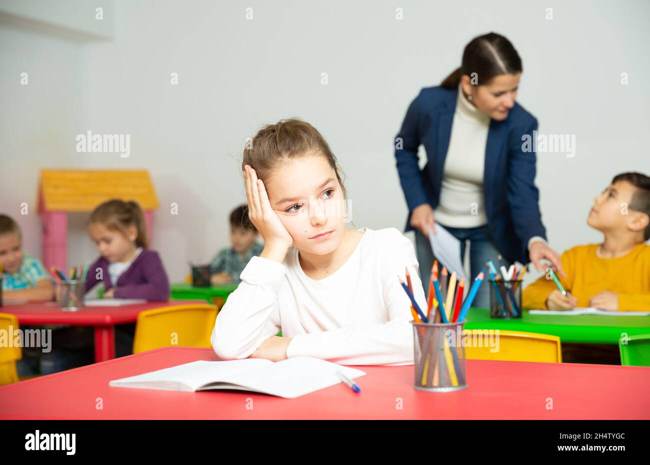 Upset schoolgirl sitting at a desk in classroom elementary school Stock ...