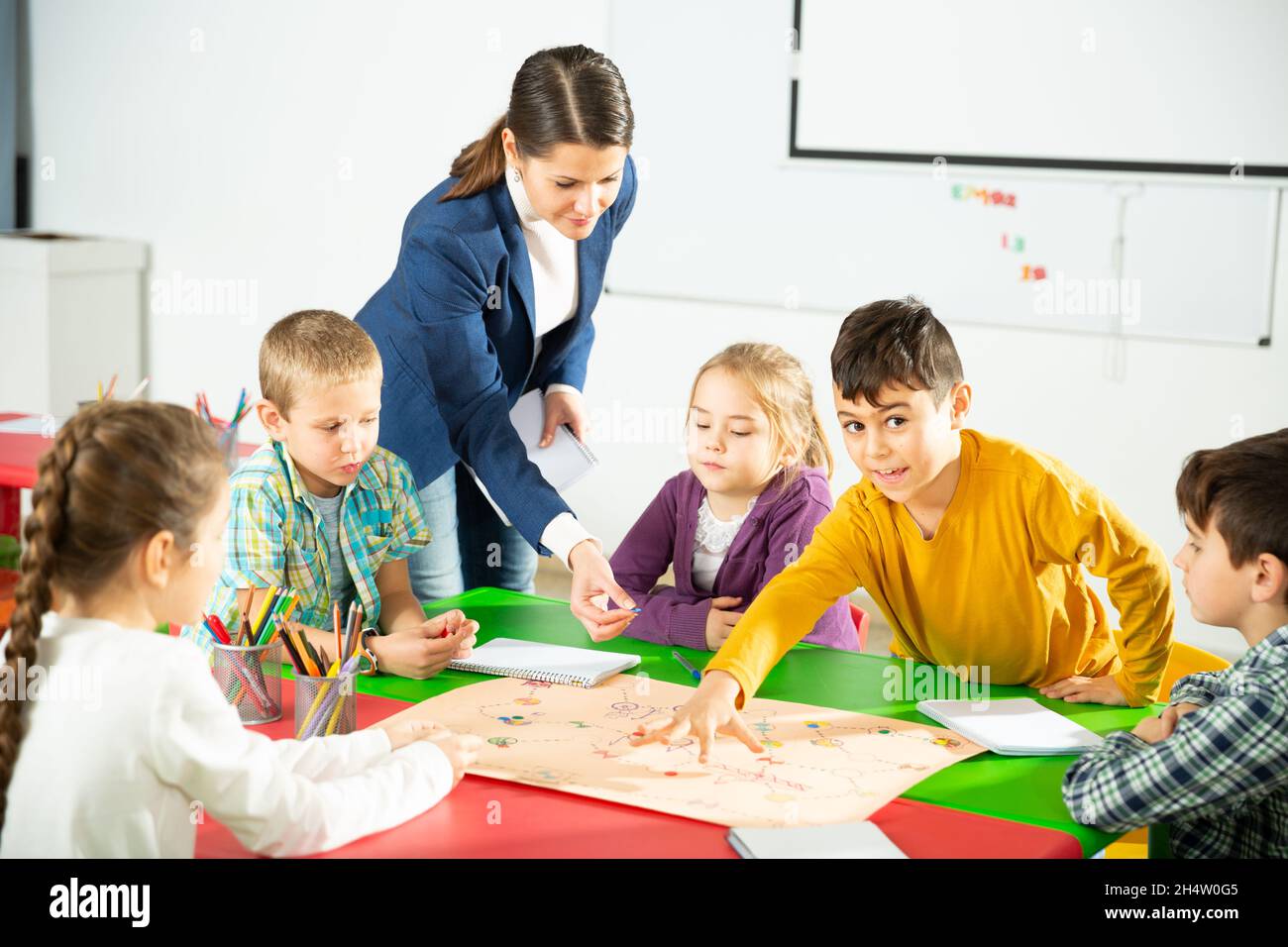 Teacher and happy children sitting at table with board game and dice in ...