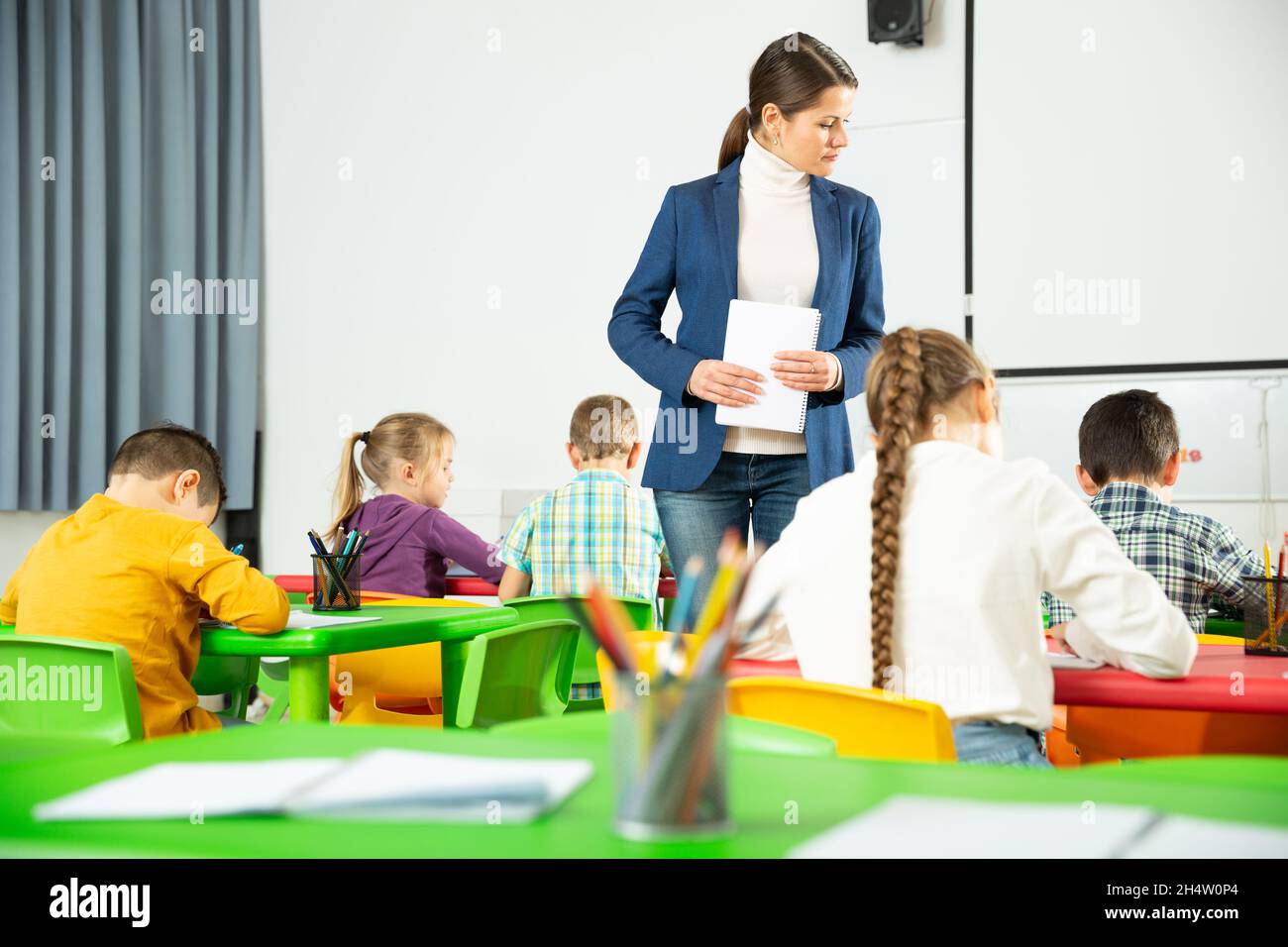 Female teacher and pupils working in classroom at elementary school ...