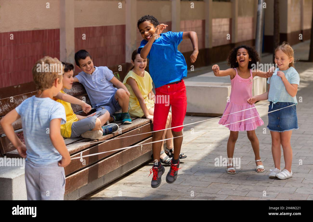 Energetic kids playing and skipping on elastic jumping rope in yard ...