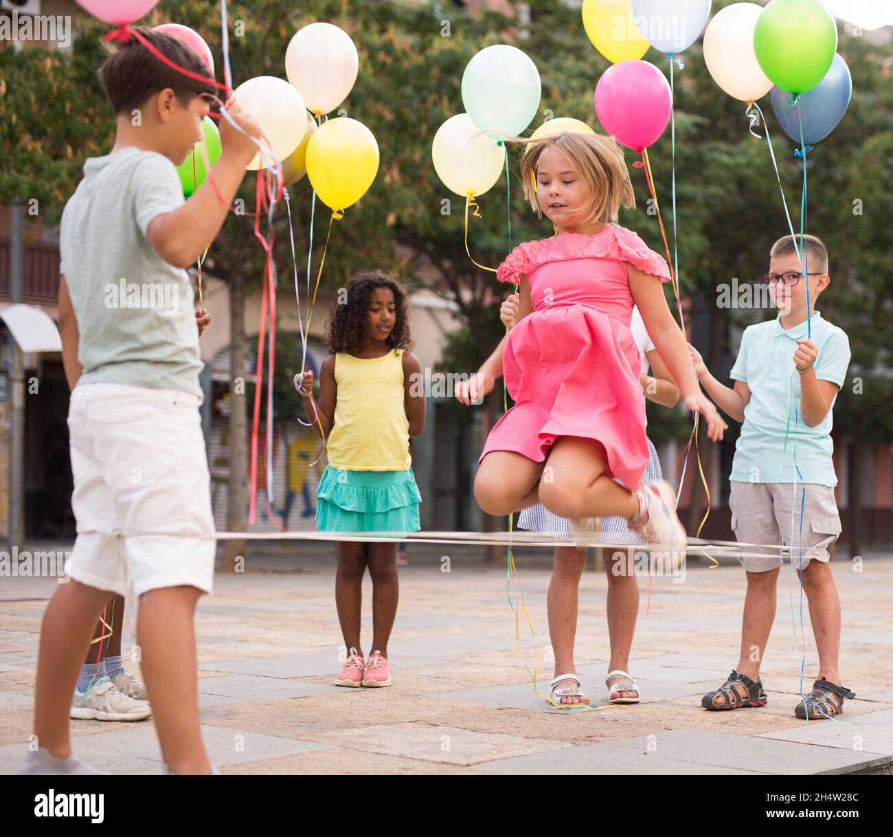 Happy preteen kids with balloons skipping on chinese jump rope in ...