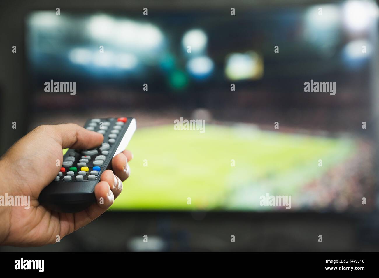 Young man holding television remote control watching football program ...