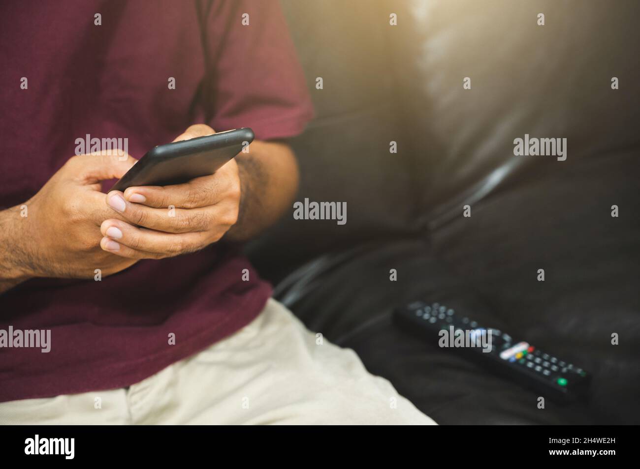 Young man holding smartphone and television remote control. Hands ...