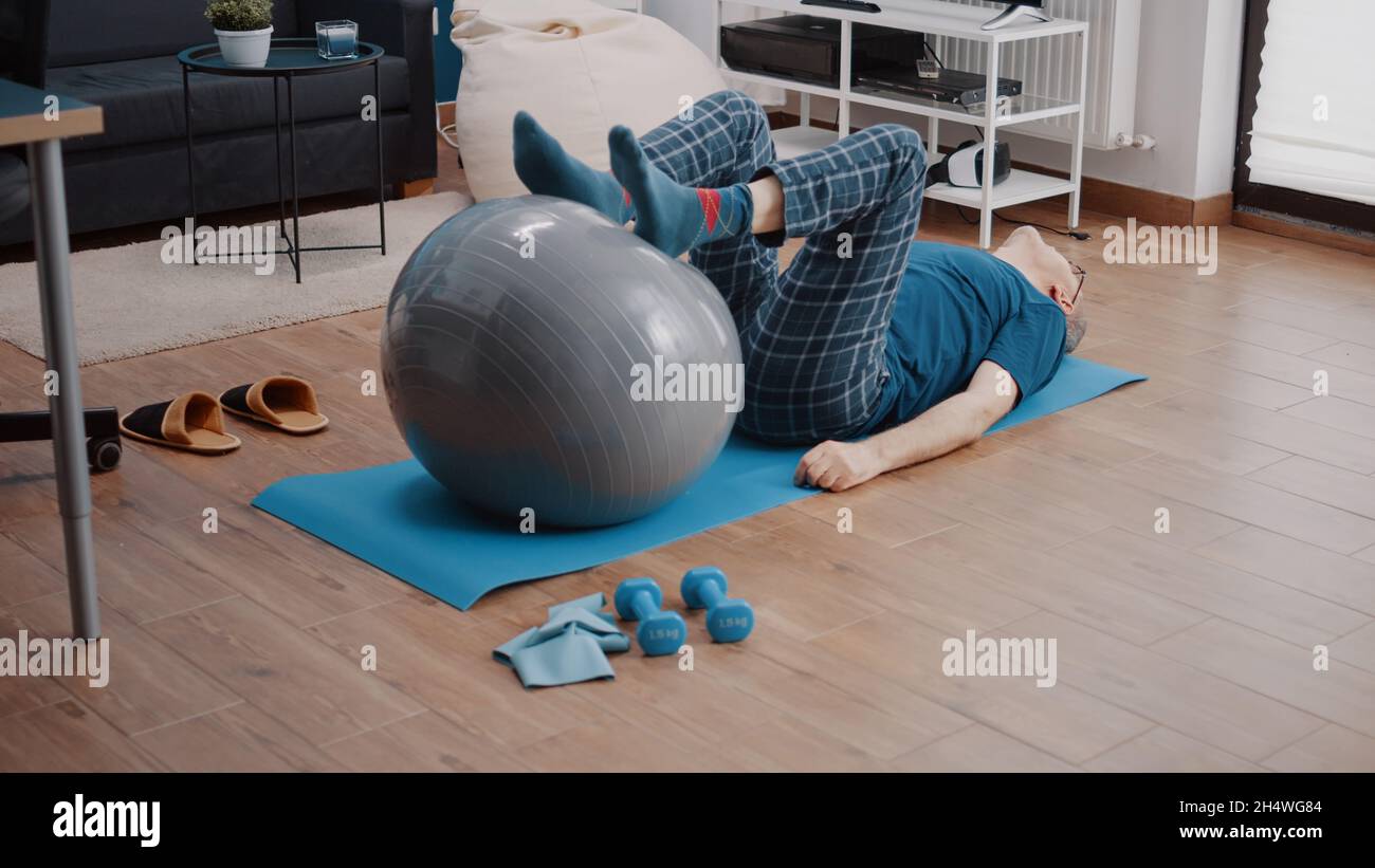 Aged person using toning ball to stretch legs muscles on yoga mat ...