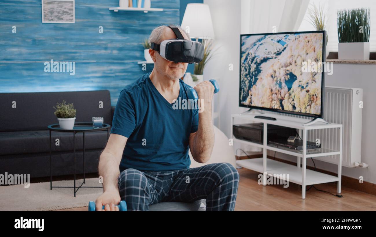 Pensioner using vr glasses to do physical exercise with dumbbells while ...