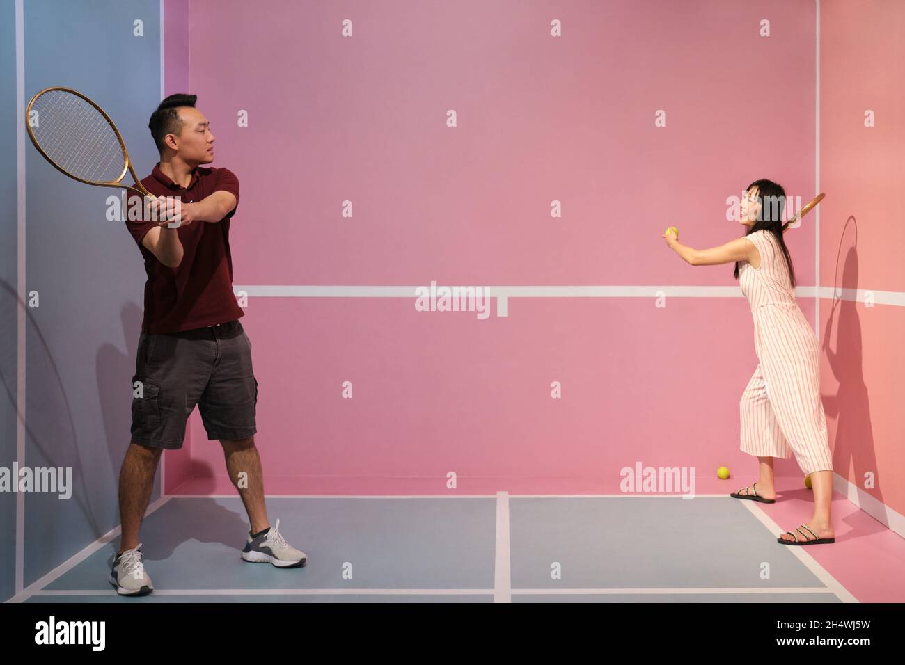 Young asian couple pretending playing tennis on a pastel pink and blue ...