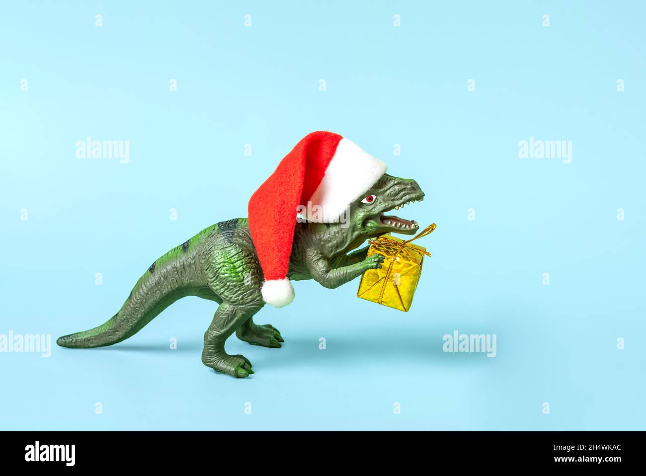 Dinosaur Rex in red Santa Claus hat holds golden gift box in its paws ...