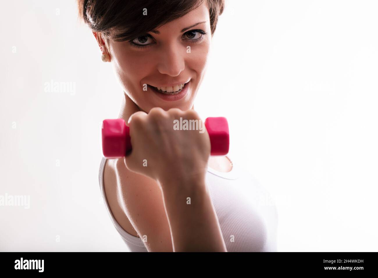 Determined young woman working out with weights lifting a dumbbell in ...