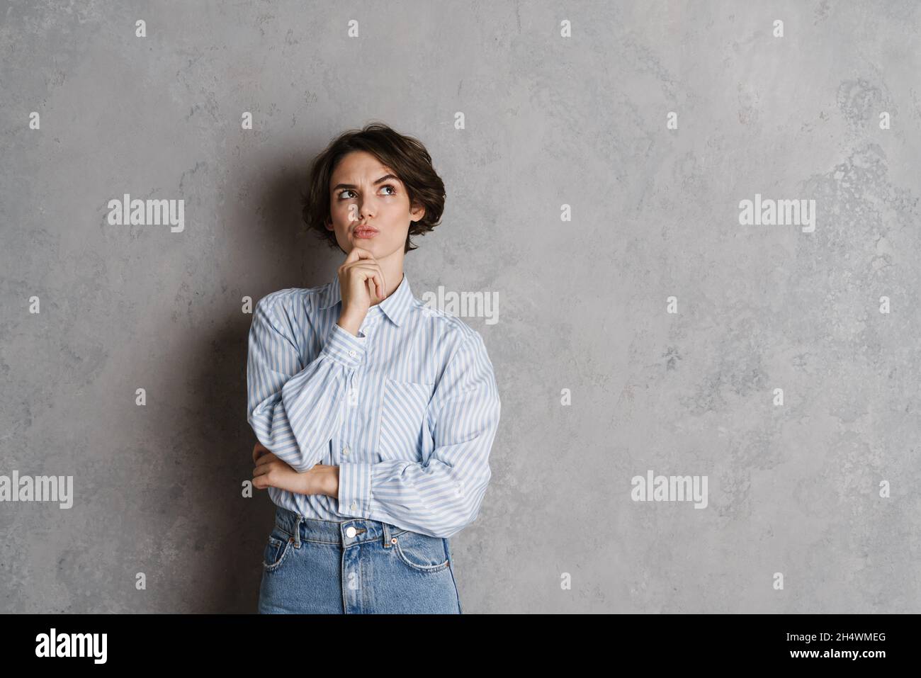 Young brunette woman holding her chin and looking upward isolated over ...