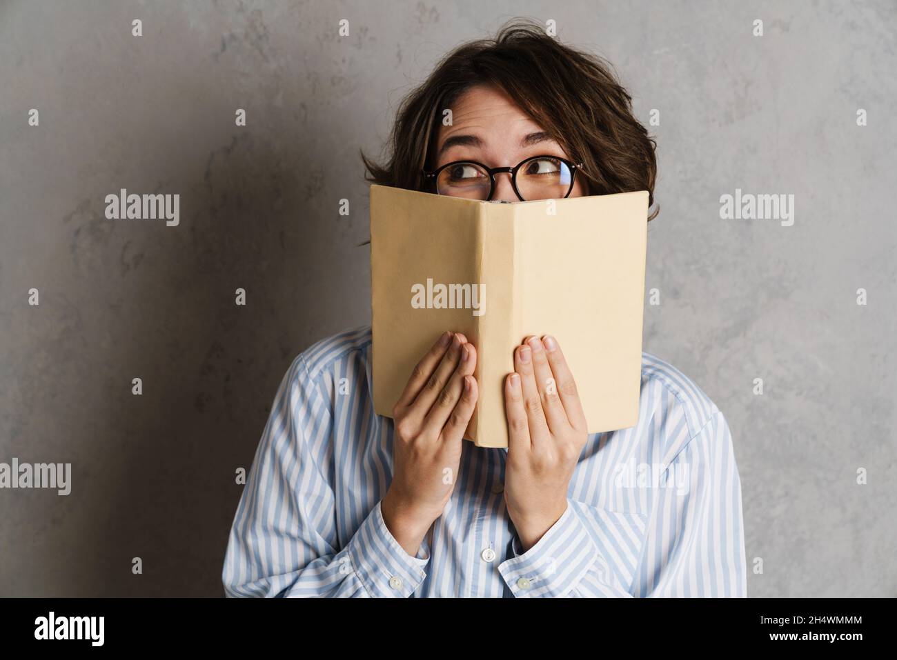 Young woman wearing eyeglasses looking aside while posing with book ...