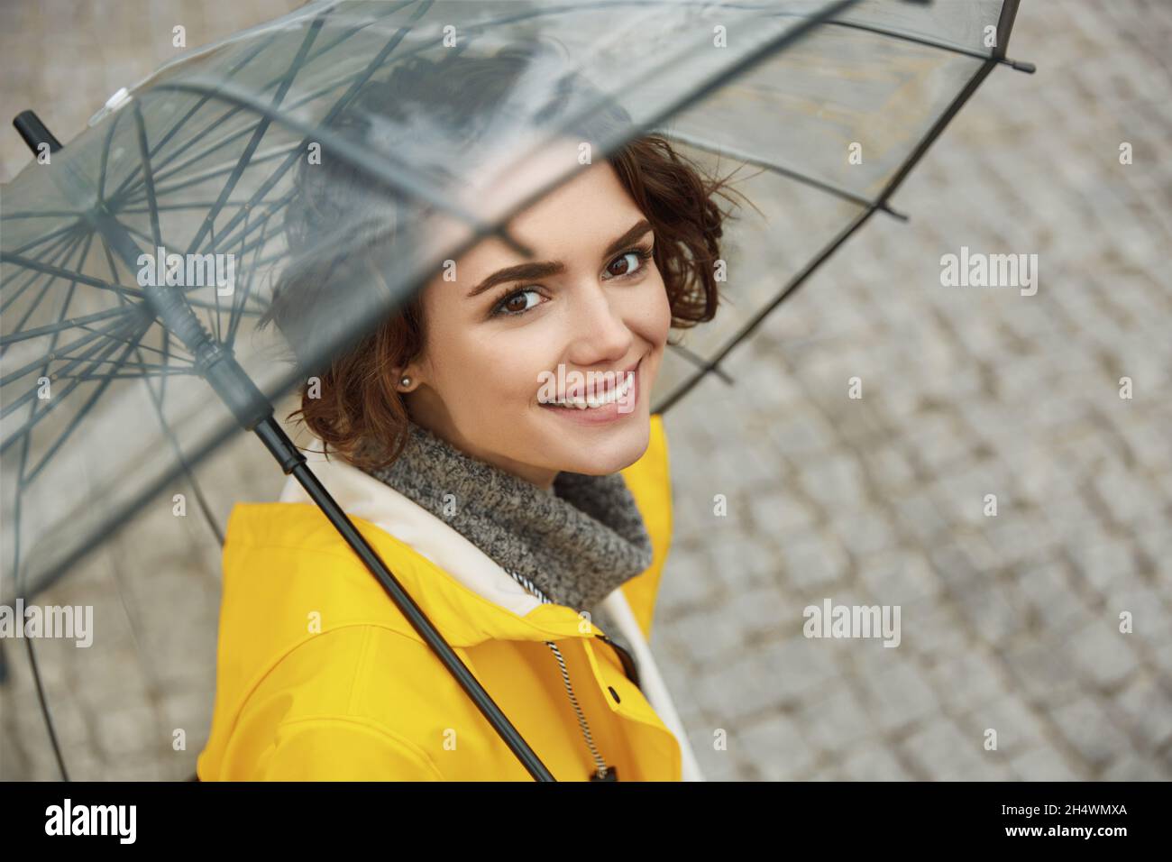 Caucasian girl in yellow raincoat with transparent umbrella in city ...