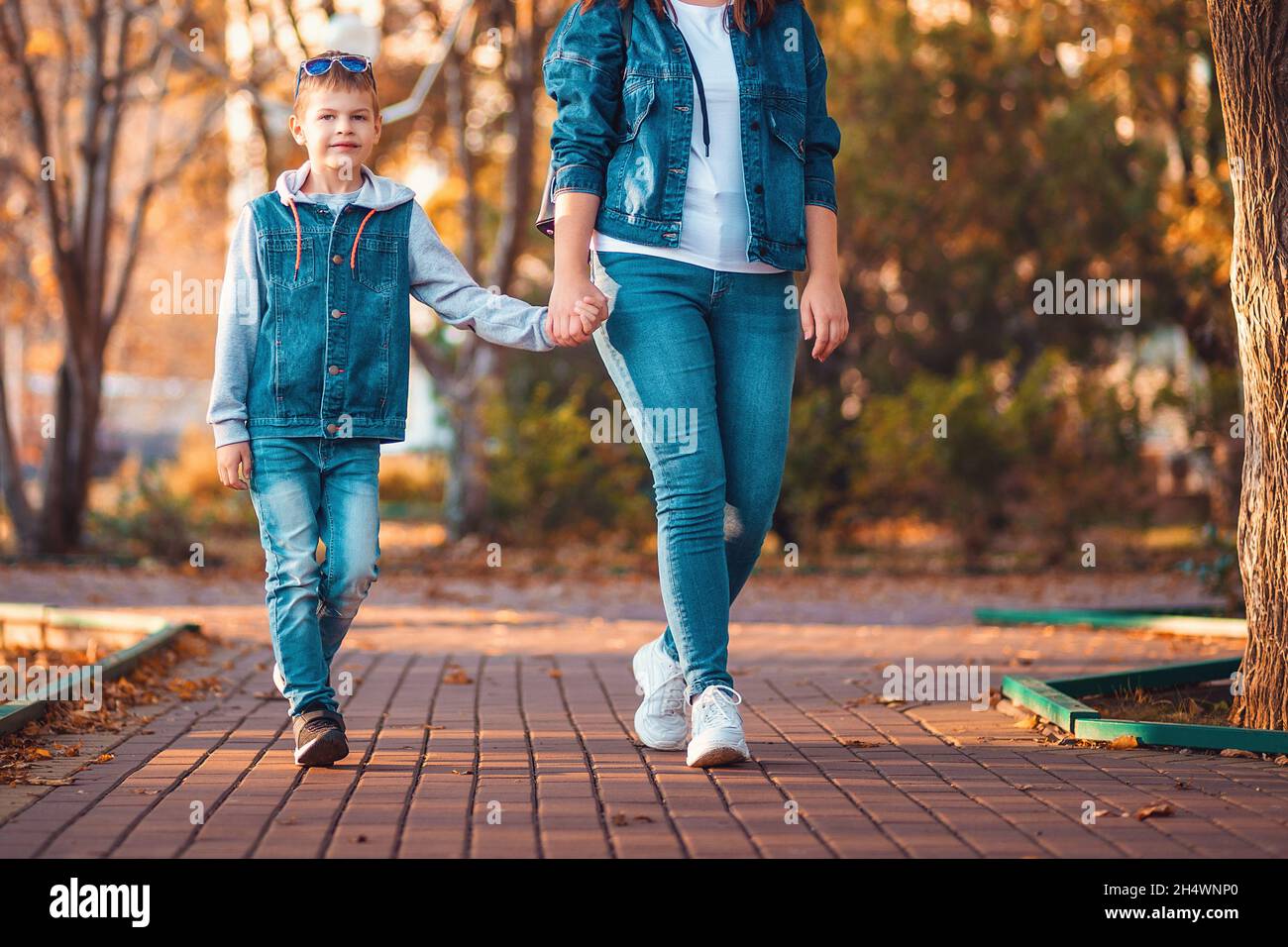 A well-mannered boy holds his mother's hand while walking together in ...