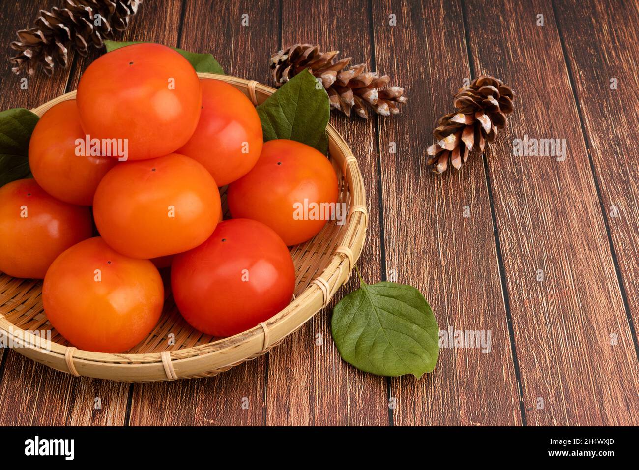 Ripe persimmons in a bamboo basket. Top view, wooden table background ...