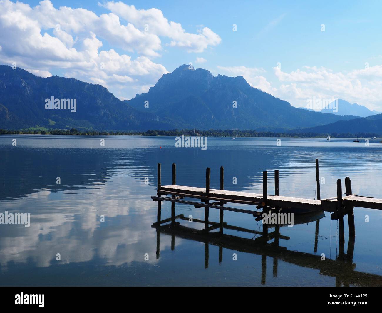 View of a wooden jetty of a calm lake, a boat, and a small sailing ship ...