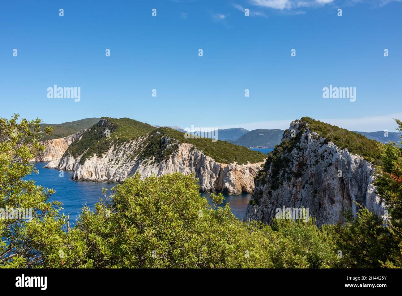 High steep rocky cliffs covered in greenery, sunny sea shore on a ...