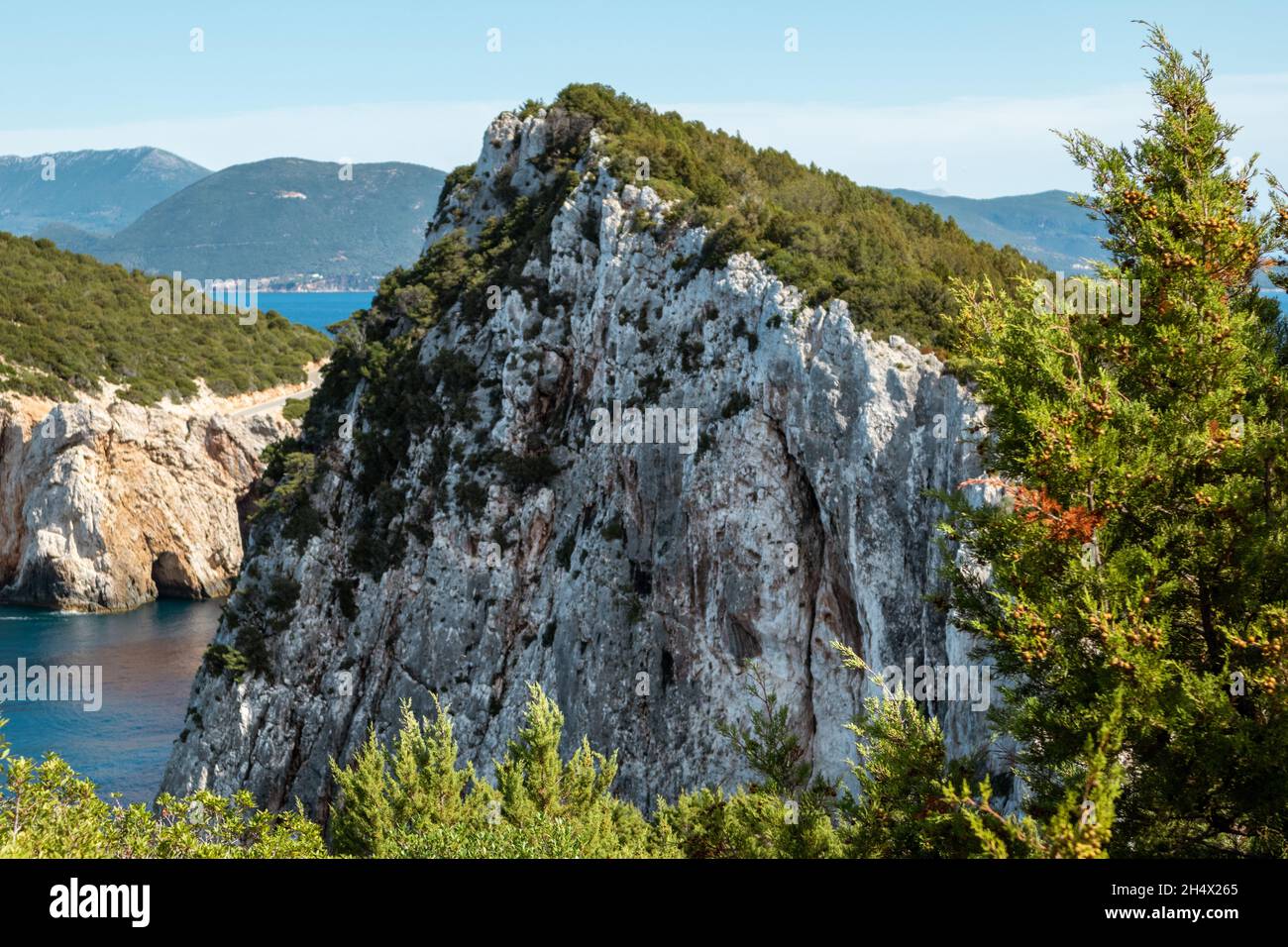 High steep rocky cliff with pine trees greenery, sunny sea shore on a ...