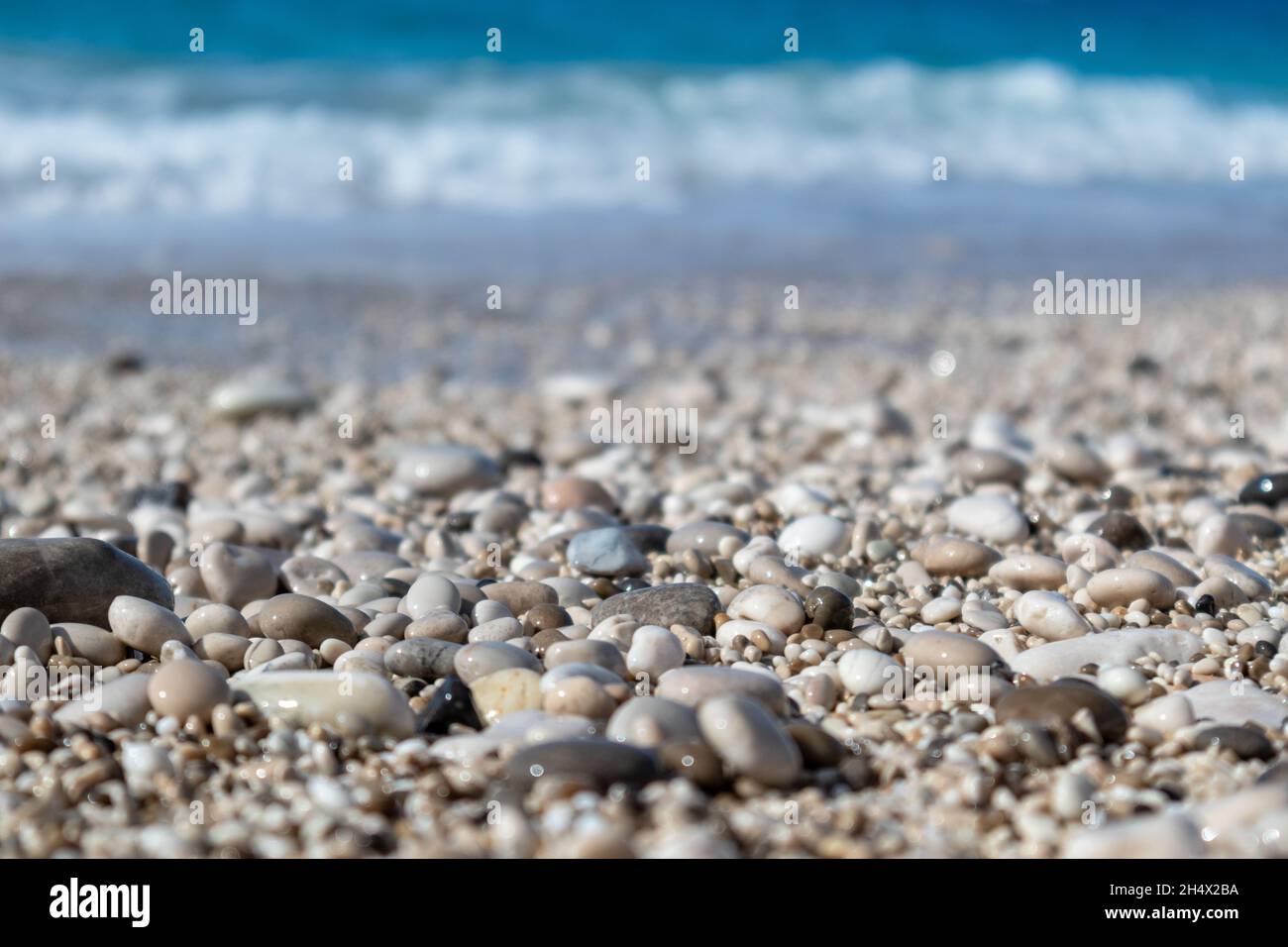 White wet pebble stones close-up on beach with blue tide waves. Coast ...