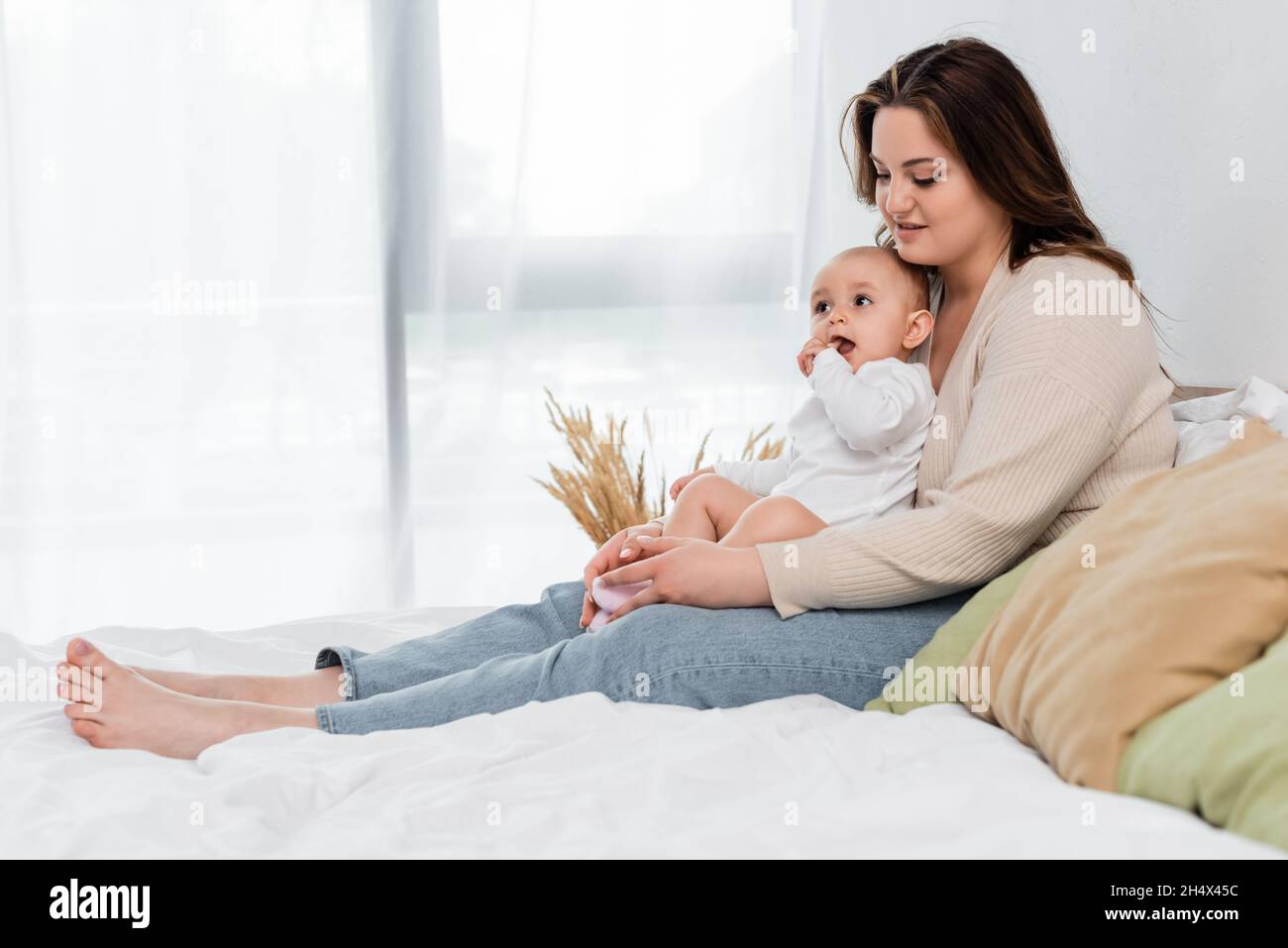 Positive body positive mother touching legs of baby daughter on bed ...