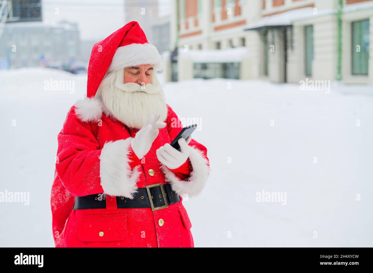 Surprised santa claus is using mobile outside. Santa Claus stands in ...