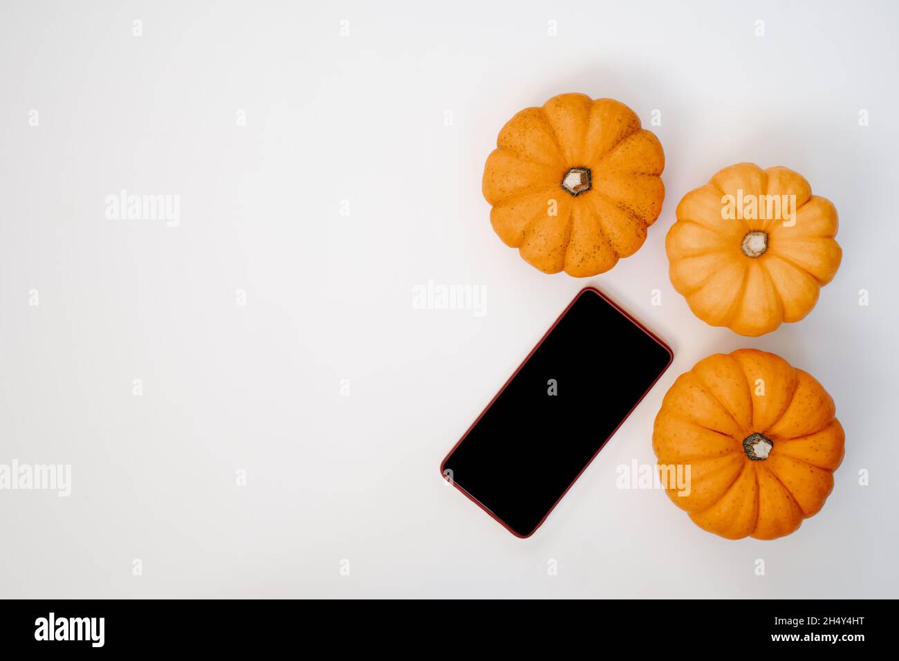 blank phone in red case and three orange pumpkins on white background ...
