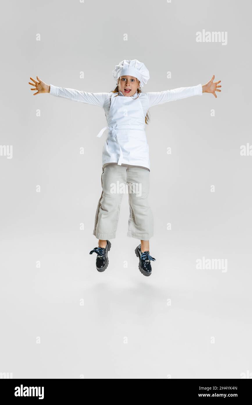 Dynamic image of little cute girl in white cook uniform and huge chef's ...