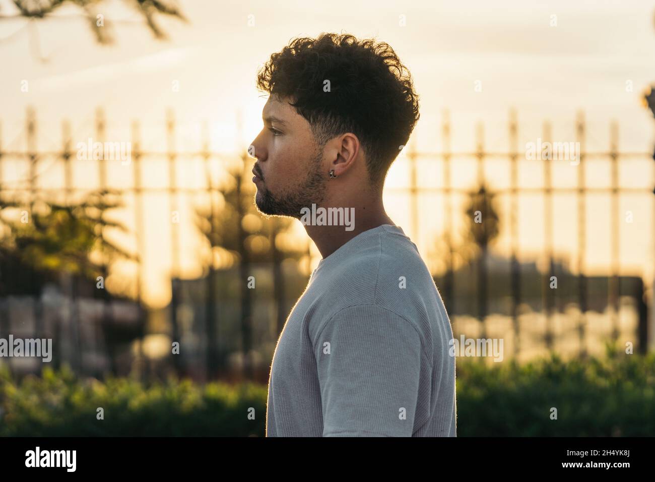 Profile of a male standing in front of the fence of a park during ...