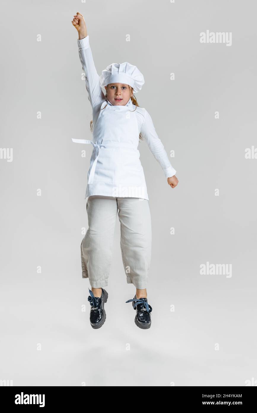 Dynamic image of little cute girl in white cook uniform and huge chef's ...