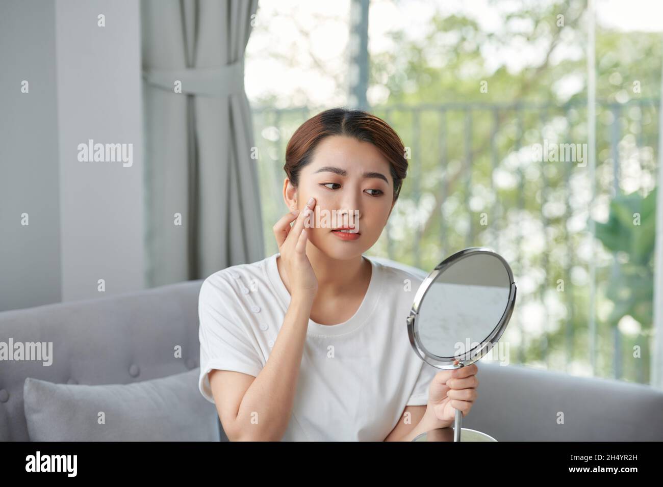 beautiful young woman examining her face in the mirror Stock Photo - Alamy