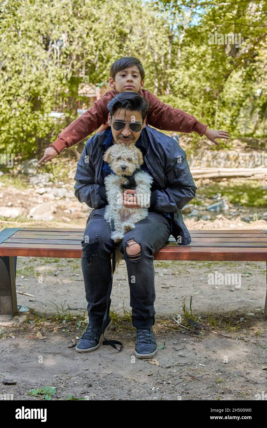 latino father and son, and a white toy poodle puppy sitting in a wooden ...